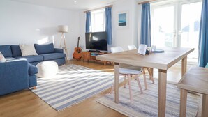 Uma sala de estar moderna com um sofá azul, uma mesa de jantar de madeira e uma TV.