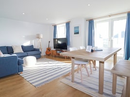 Uma sala de estar moderna com um sofá azul, uma mesa de jantar de madeira e uma TV.
