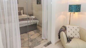 Quarto com cama, porta de vidro, luminária e sofá com almofadas estampadas.