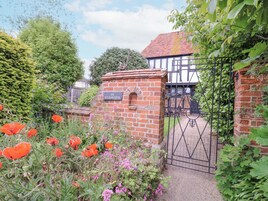 Um portão de tijolo com uma placa indicando "14 St David's" dá acesso a um edifício em estilo Tudor com telhado em telhas.