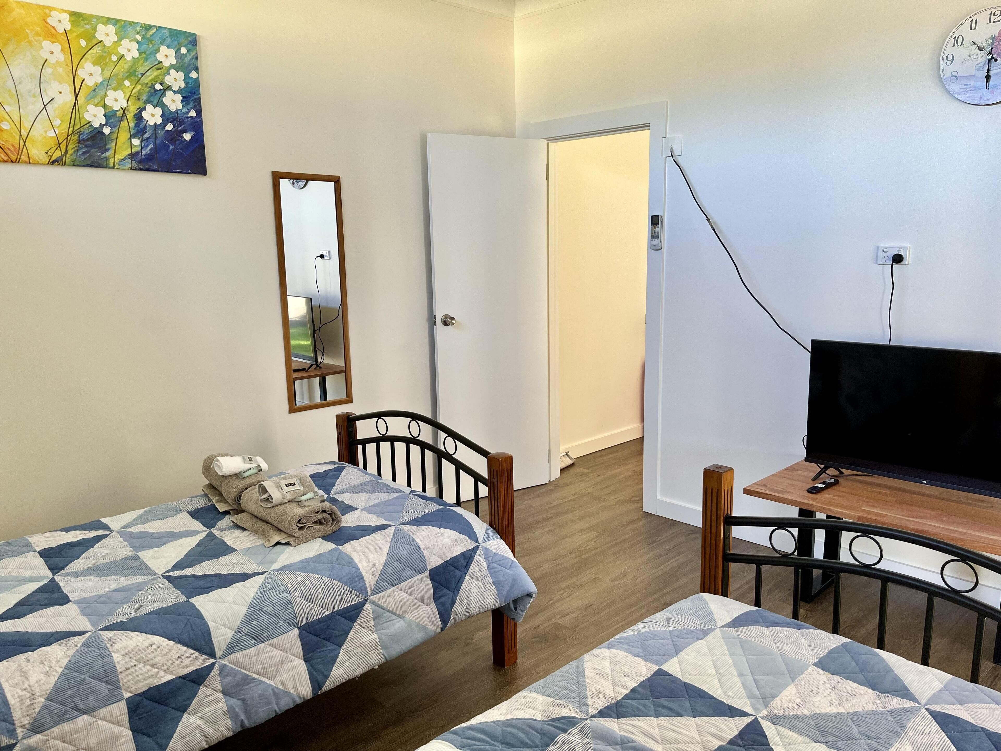 Quarto com duas camas, uma escrivaninha com televisão, um espelho e um quadro na parede.