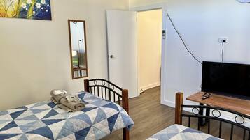 Quarto com duas camas, uma escrivaninha com televisão, um espelho e um quadro na parede.