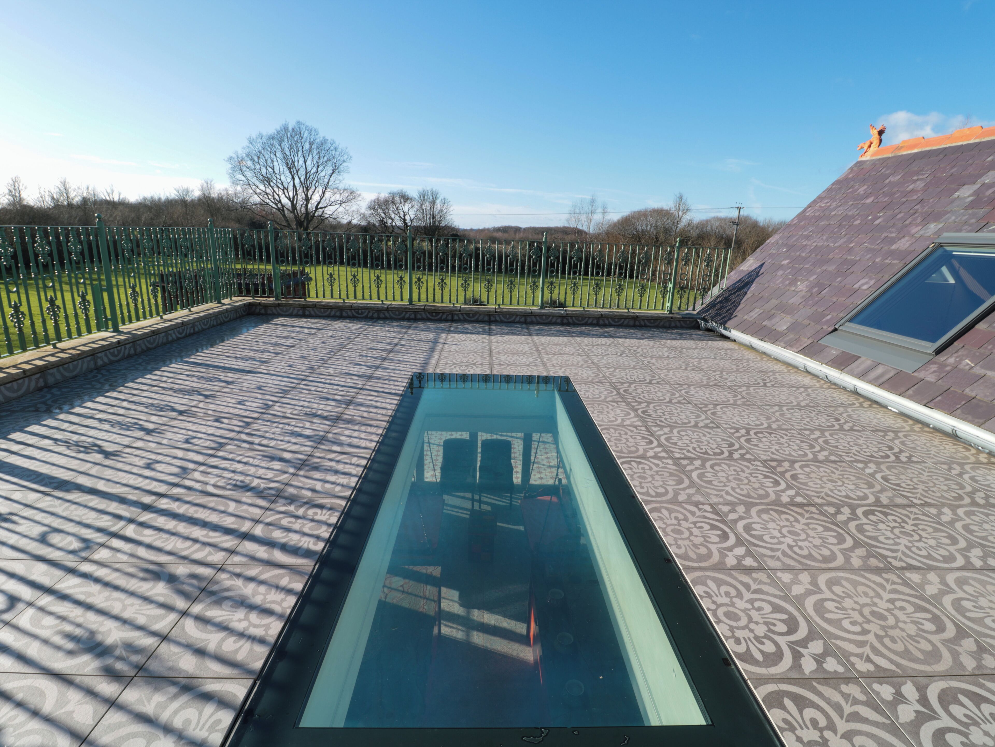 Piscina no terraço com azulejos estampados, cerca verde e céu limpo.