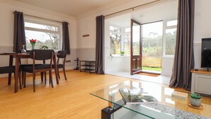 Uma sala de estar ampla com uma mesa de centro de vidro, piso de madeira, uma mesa de jantar com cadeiras e um móvel para TV.