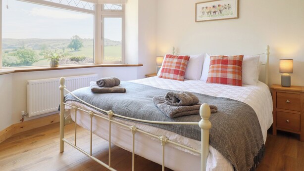 Quarto com cama, janela com vista para o campo, mesa de cabeceira com luminária e quadro pendurado na parede.