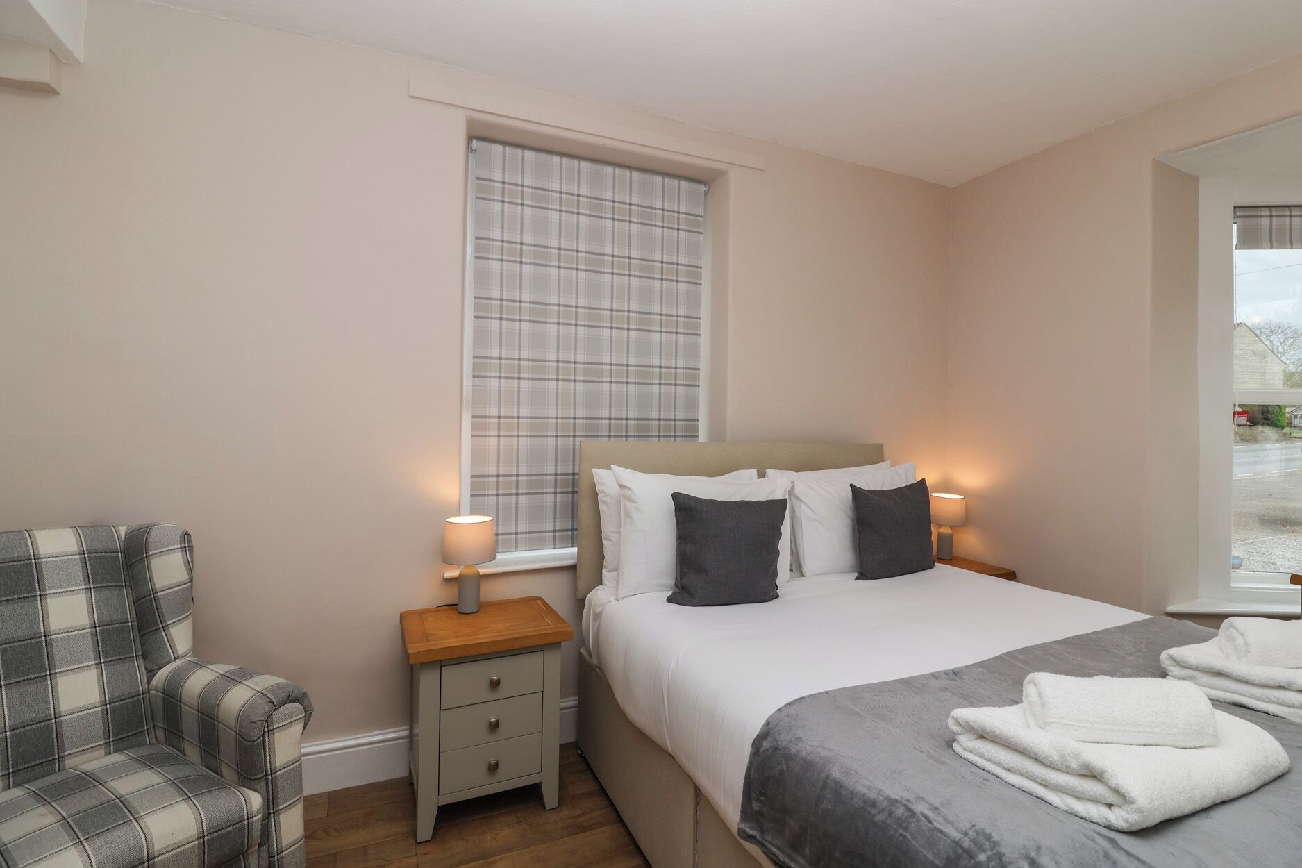 Quarto com cama, mesa de cabeceira, cadeira e janela com persianas.