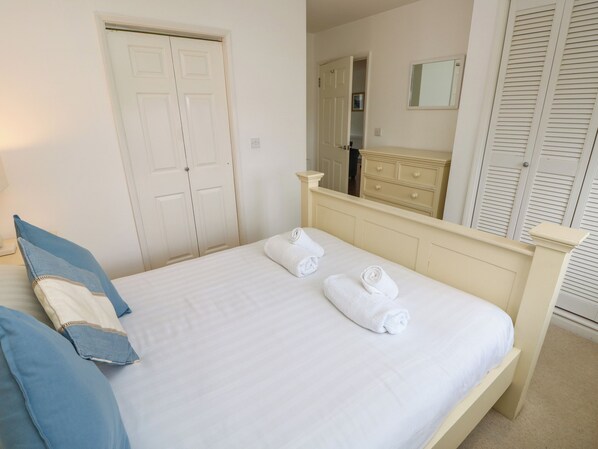 Cama bem arrumada com lençóis brancos e duas toalhas enroladas, um travesseiro azul e fronha azul combinando.