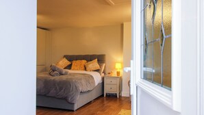 Quarto com cama, mesa de cabeceira, luminária e janela com detalhe decorativo no vidro.
