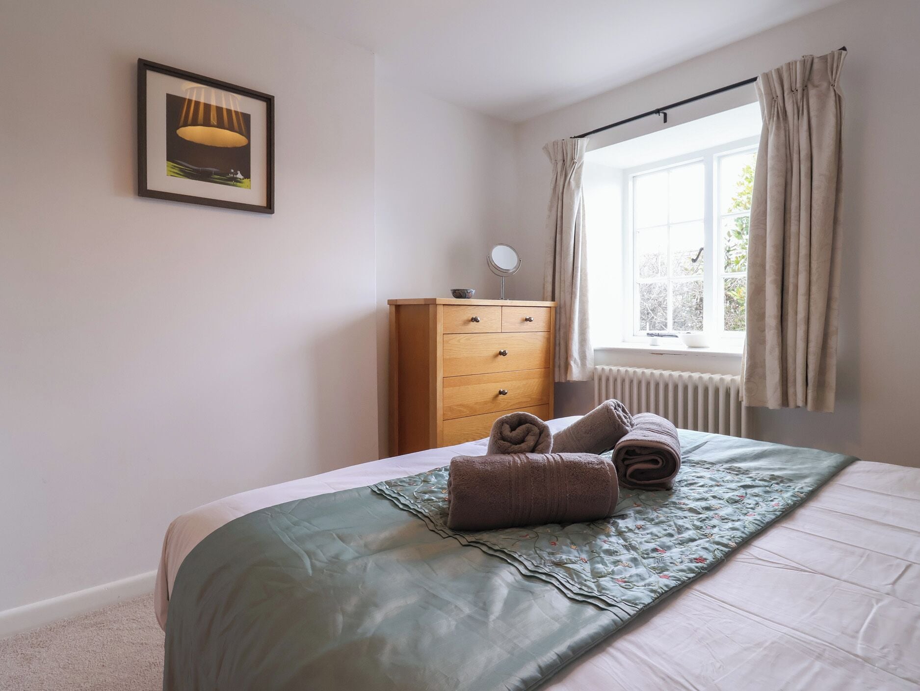 Quarto com uma cama, cômoda de madeira, janela com cortinas e um quadro na parede.