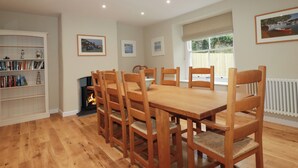 Uma sala de jantar com mesa e cadeiras de madeira, uma estante de livros e quadros nas paredes.