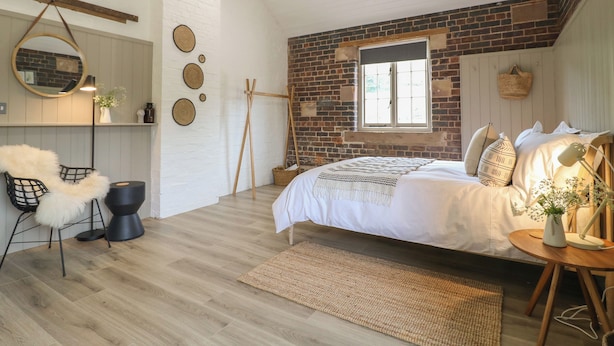 Quarto com parede de tijolos, cama grande, cadeira suspensa e espelho redondo.