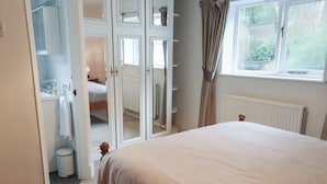 Quarto com cama grande, armário com espelhos, radiador e janela com cortinas.