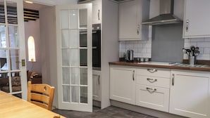 Uma cozinha moderna com armários brancos, uma mesa de jantar de madeira e um chão de azulejos cinzas.