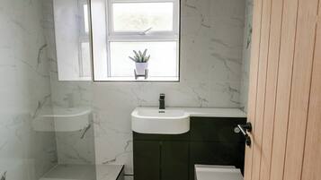 Casa de banho com lavatório branco, armário escuro e janela com planta em vaso.