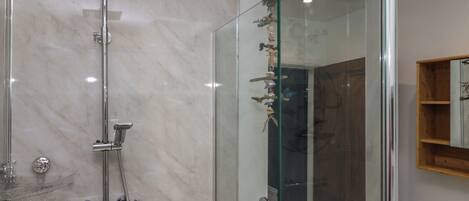 Uma casa de banho moderna com chuveiro envidraçado, parede de mármore e armário de madeira.