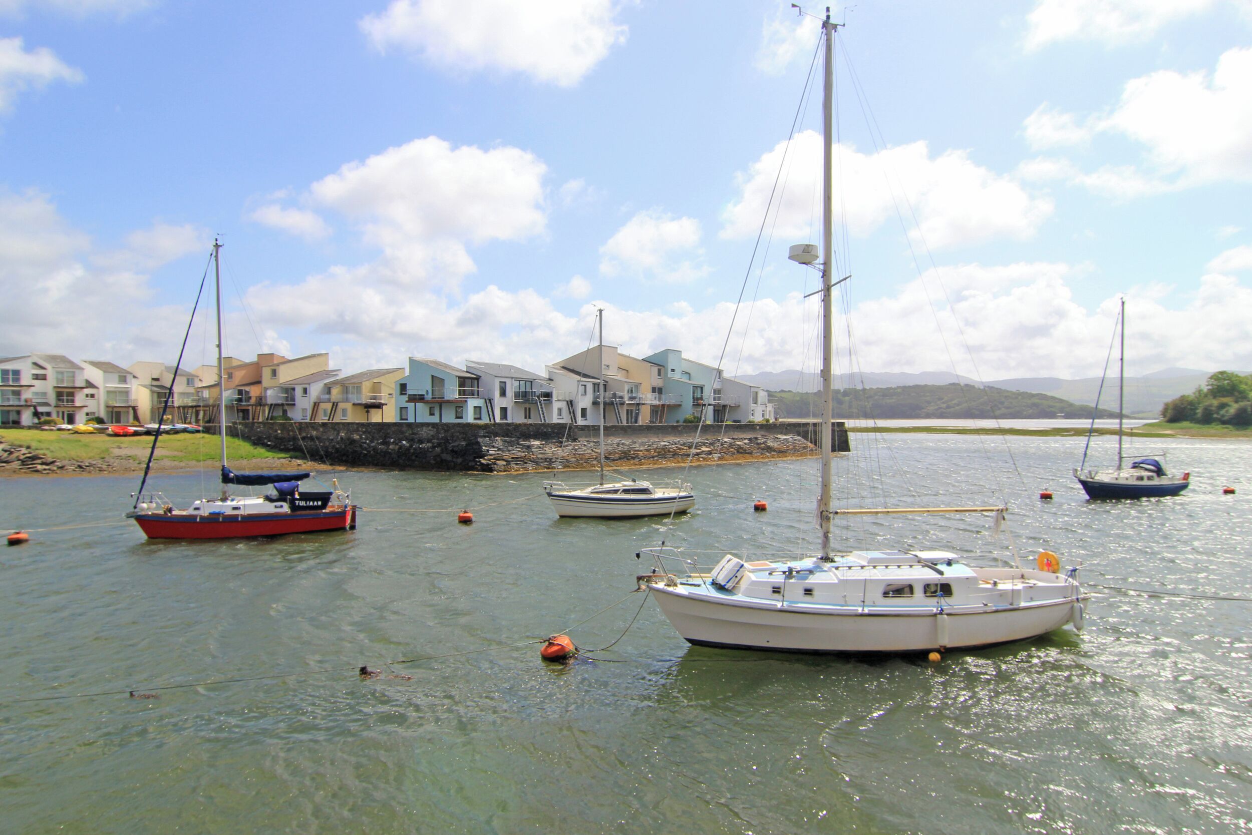 Uma marina com vários barcos ancorados, um cais e edifícios ao fundo.