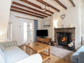 Uma sala de estar acolhedora com lareira de pedra, vigas de madeira, televisão e sofás listrados.