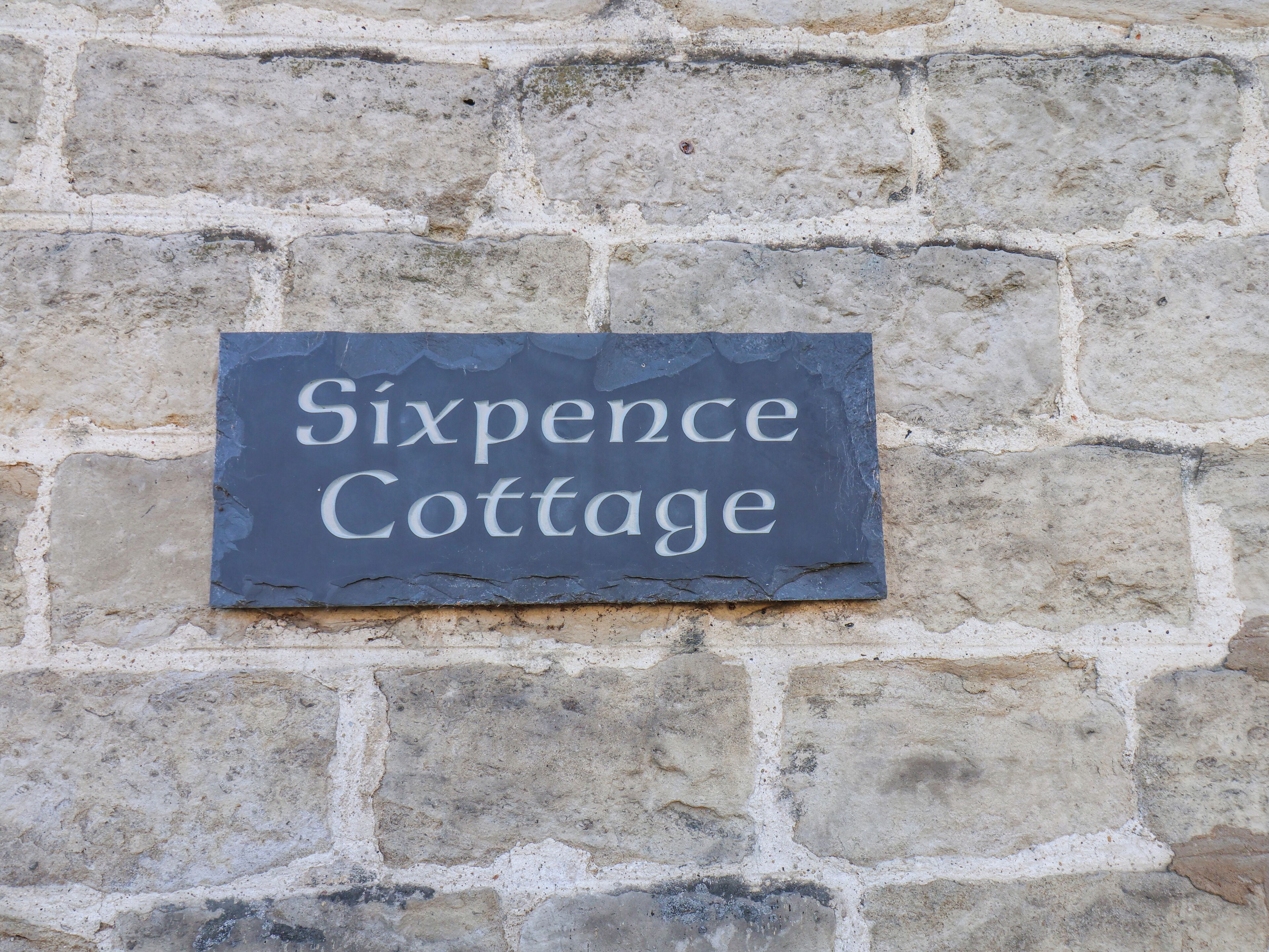 Um muro de pedra com uma placa que diz 'Sixpence Cottage'.