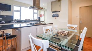 Uma cozinha moderna com ilha central, armários brancos e mesa de jantar de vidro com cadeiras brancas.