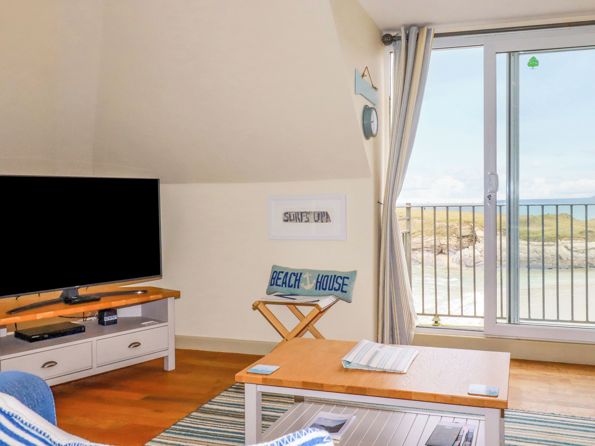 Uma sala de estar com televisão, cafeteira, uma mesa pequena e um letreiro que diz "BEACH HOUSE".