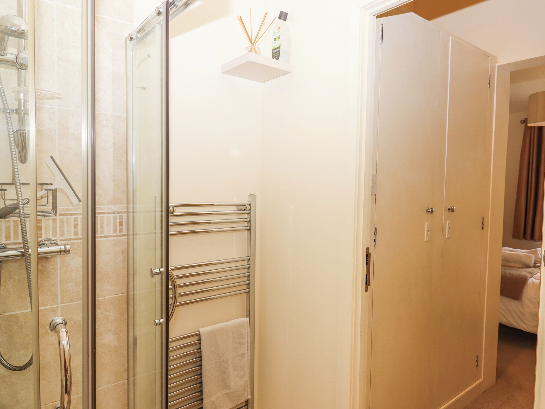Quarto de hotel com box de vidro, porta-toalhas com toalha e guarda-roupa com duas portas.