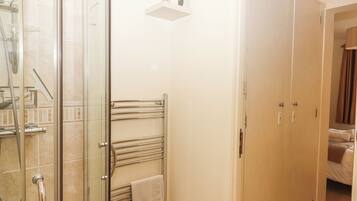 Quarto de hotel com box de vidro, porta-toalhas com toalha e guarda-roupa com duas portas.