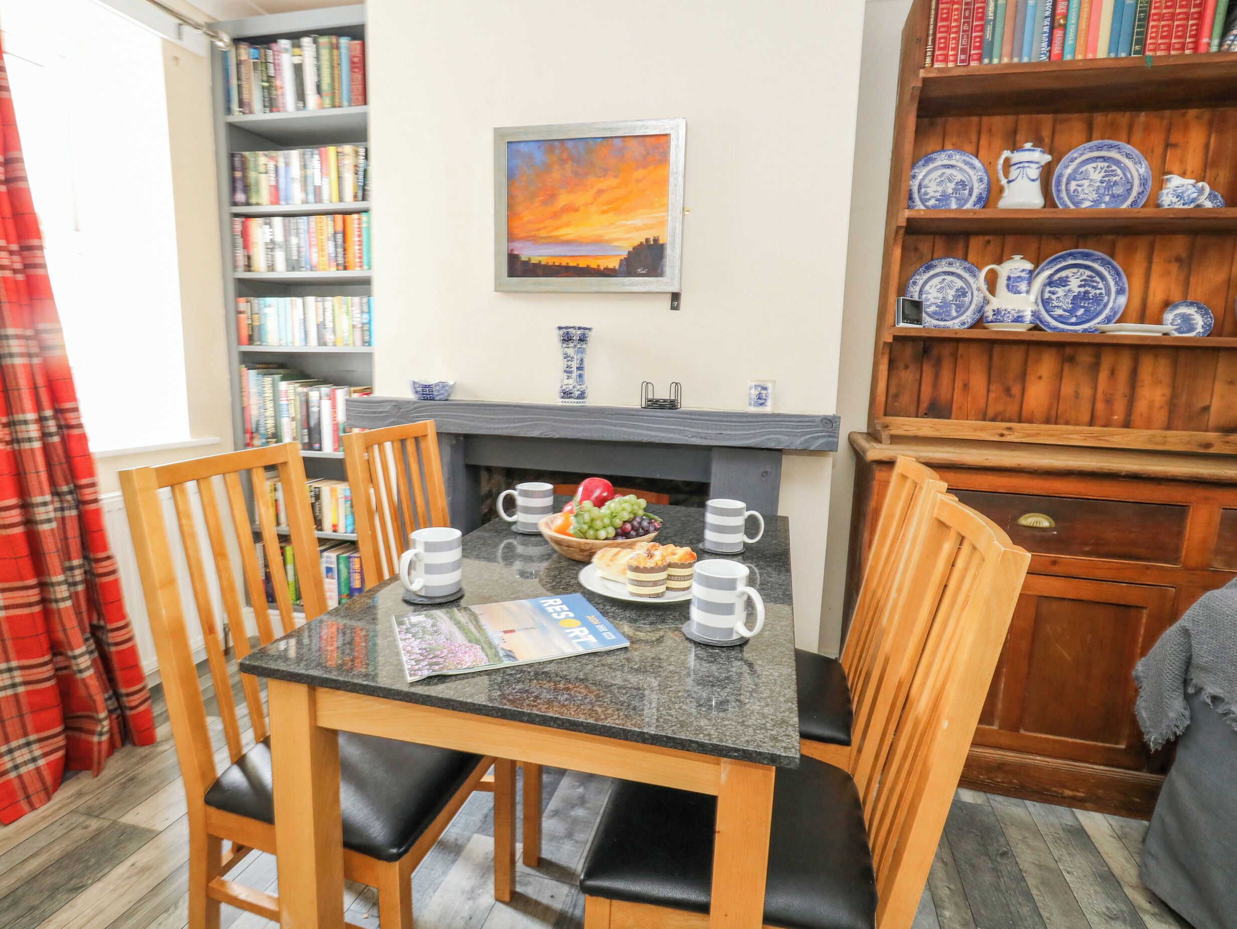 Uma sala de jantar com uma mesa posta para dois, uma estante de livros, uma lareira e um aparador decorativo.