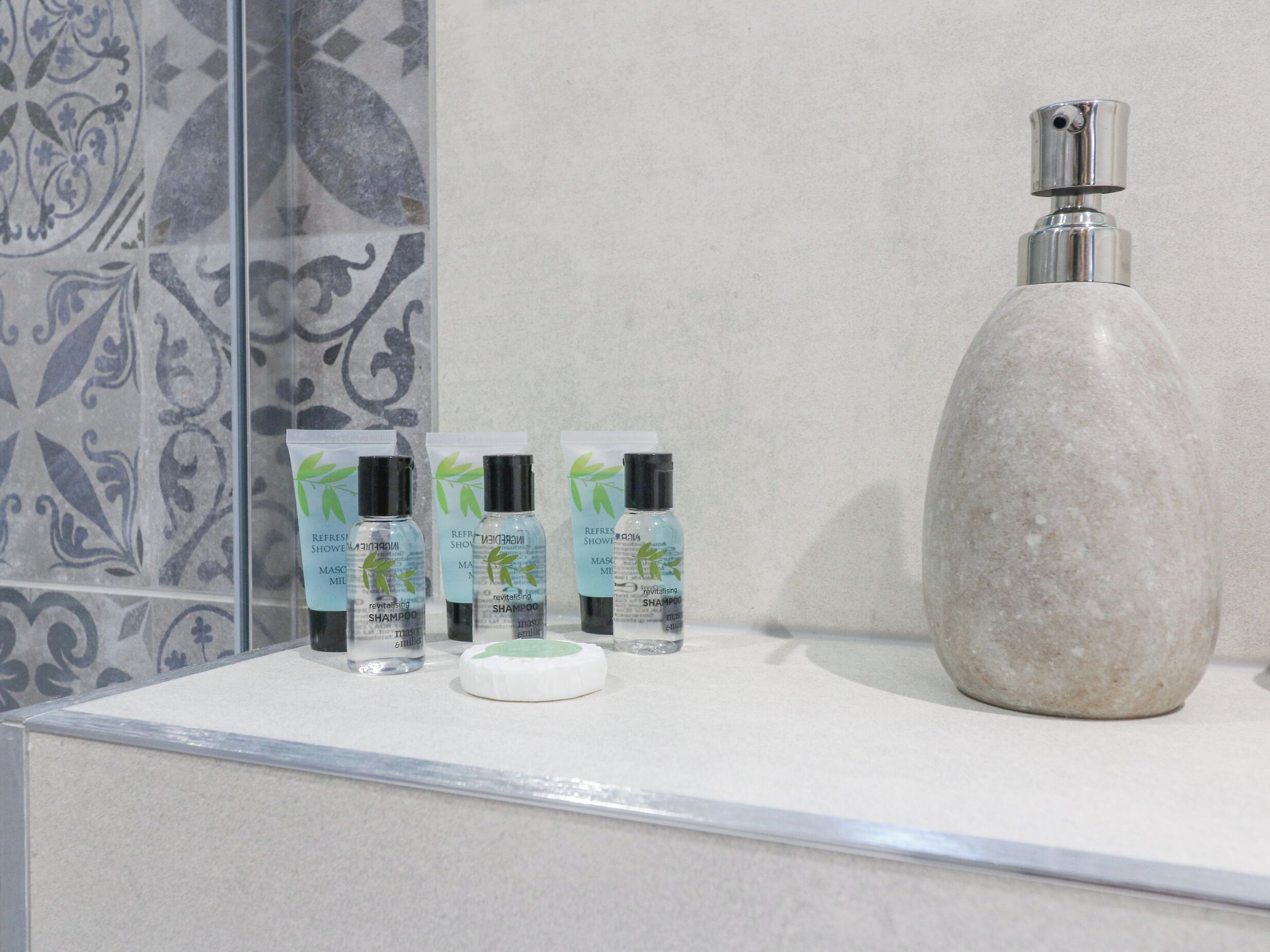 Uma bancada de banheiro com três frascos de Shampoo Revitalizante, uma embalagem de shampoo com bomba e um saboneteira.