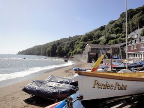 Uma praia com um barco chamado 'Penlee Point' e um edifício com uma placa 'Penlee Point'.