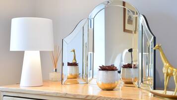 Um espelho com decoração de girafa dourada, uma luminária branca e três vasos de vidro com suculentas em uma cômoda de madeira.