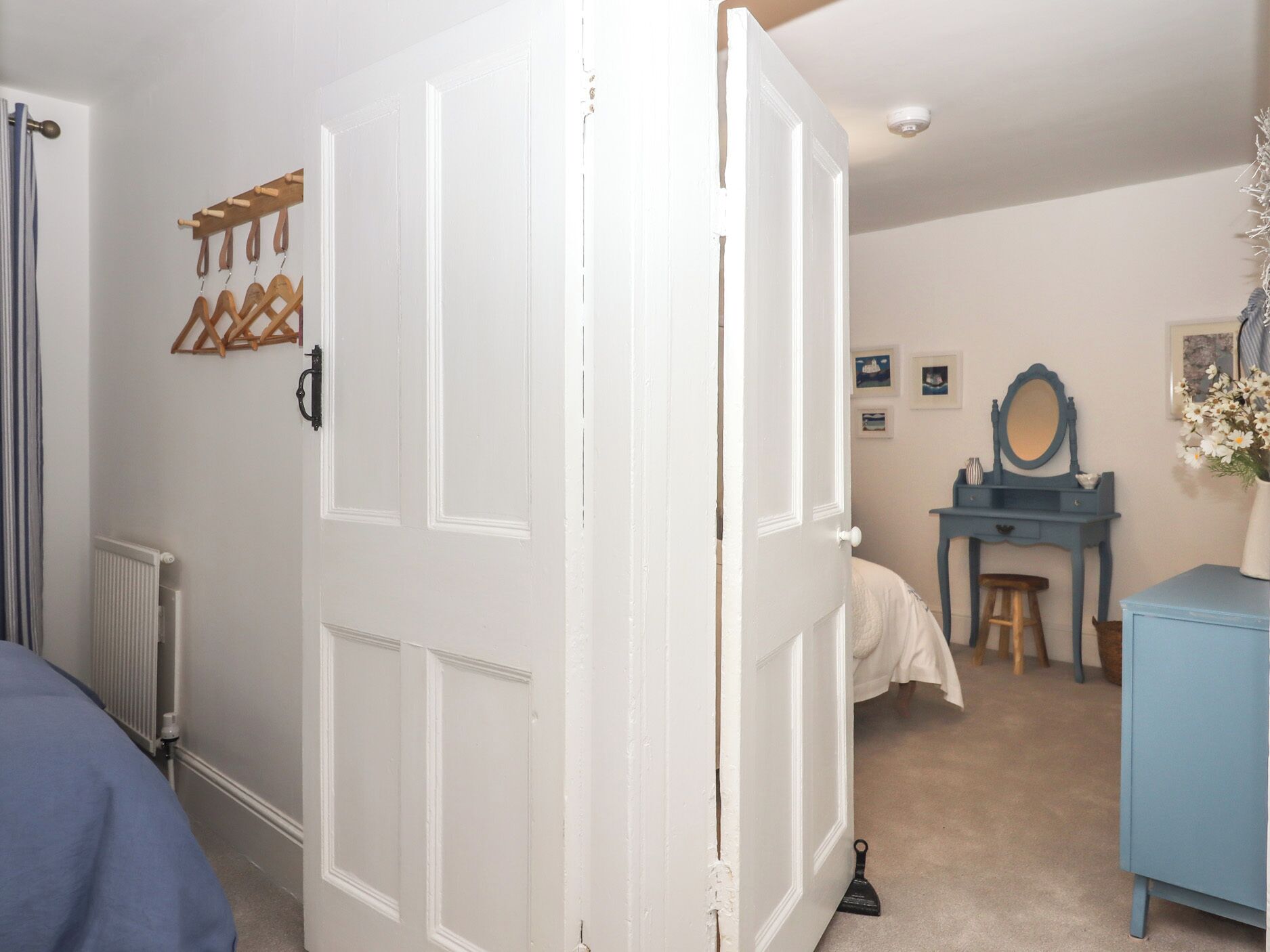 Quarto com porta branca, cómoda azul, toucador com espelho e radiador.