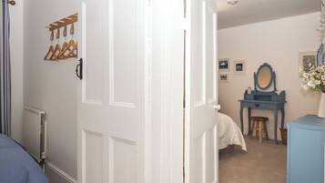 Quarto com porta branca, cómoda azul, toucador com espelho e radiador.