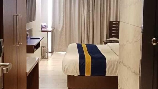 Quarto de hotel com cama, escrivaninha, televisão e janela com cortinas.