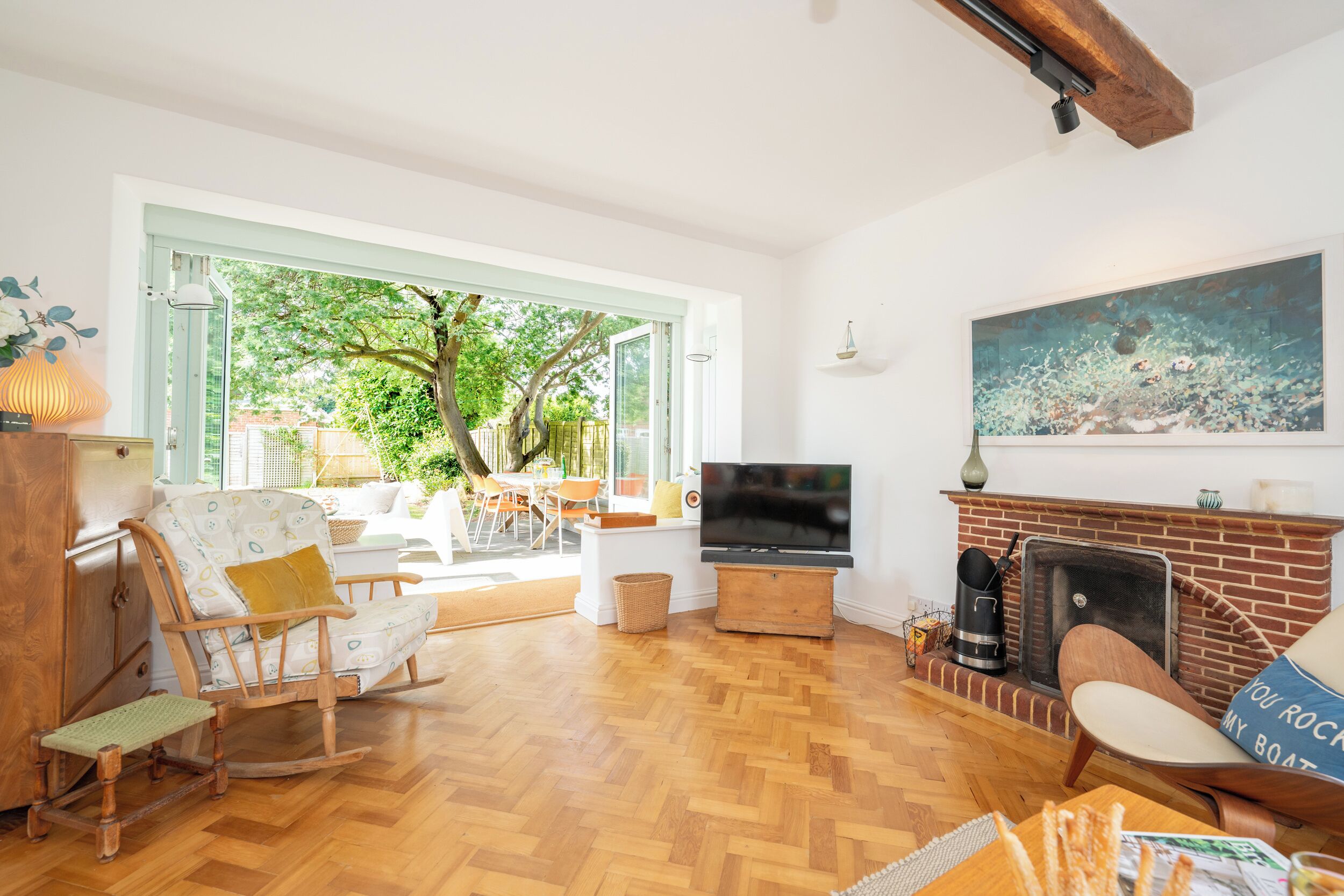 Sala de estar com piso em padrão herringbone, televisão, lareira e vista para o exterior.