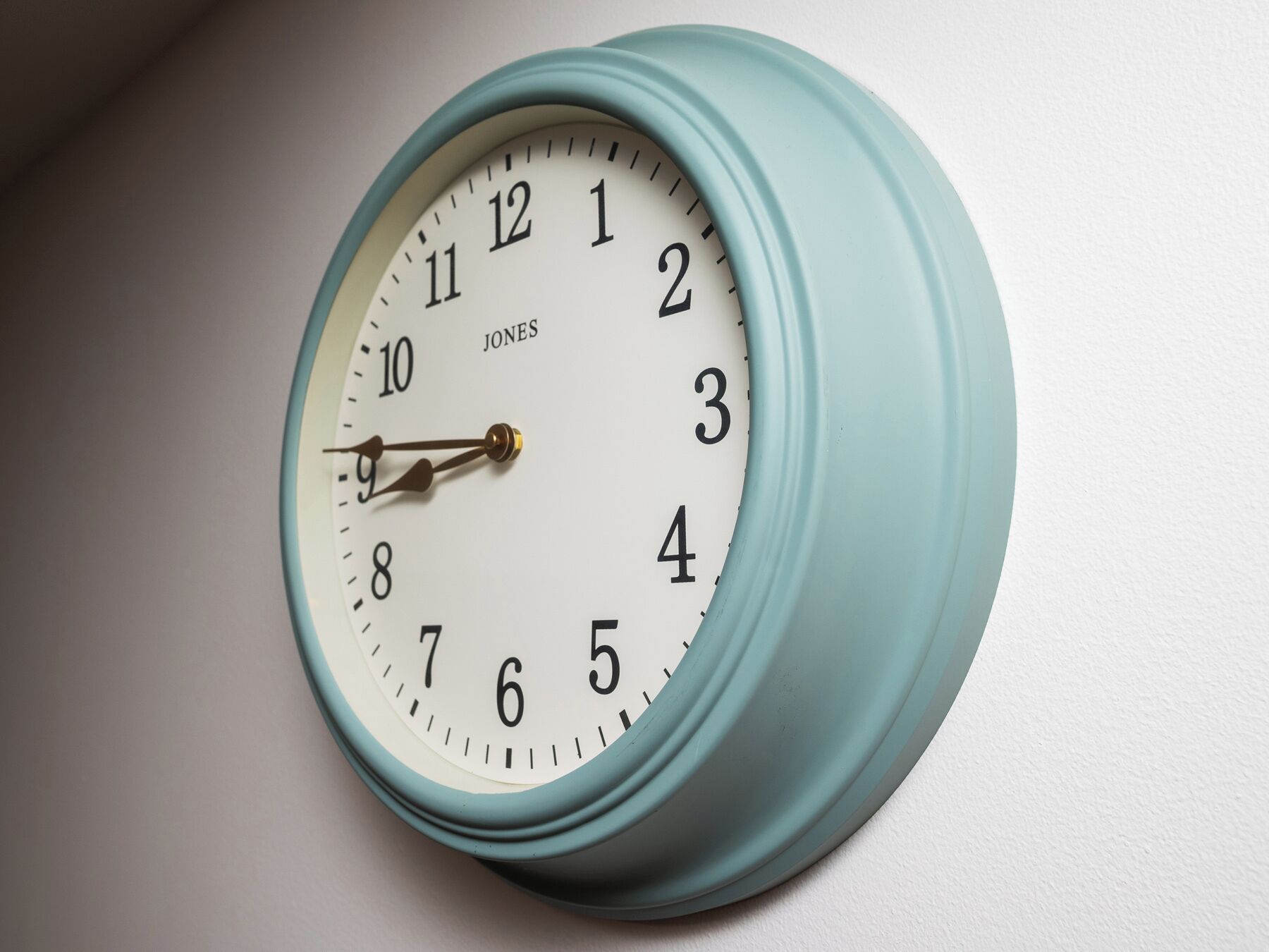 Um relógio de parede com mostrador branco e moldura verde-água, marcando aproximadamente 8:45.