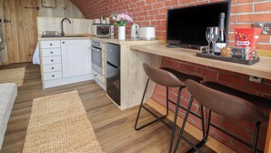 Uma cozinha compacta com parede de tijolos, armários de madeira, forno embutido e um pequeno espaço bar com bancos.