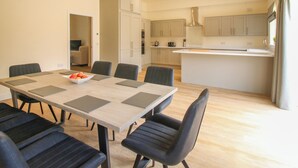 Uma cozinha moderna com uma ilha central, uma sala de jantar com mesa e cadeiras, e uma área de estar separada com um sofá.