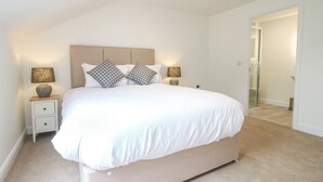 Uma cama grande com cabeceira bege, duas mesas de cabeceira com abajures e almofadas decorativas estampadas.