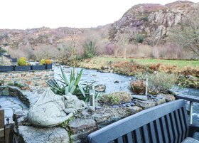 Um banco de pedra com vista para um jardim com um riacho, cercado por pedras e plantas.