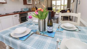 Uma área de refeições com uma mesa posta para dois, uma garrafa de vinho e um vaso de tulipas.