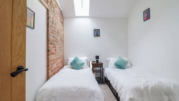 Quarto com duas camas de solteiro, porta de madeira, parede de tijolos e um claraboia.