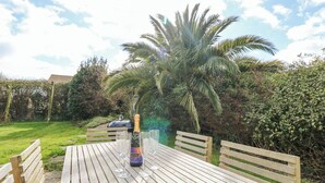 Mesa de madeira com garrafa de champanhe e copos, montada ao ar livre com uma palmeira e jardim ao fundo.