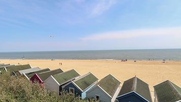 Bungalôs de praia com telhados inclinados, uma praia arenosa e o mar ao fundo.