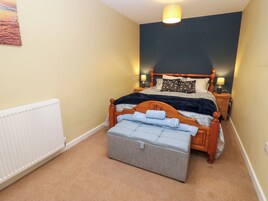 Quarto com cama, luminárias de cabeceira, radiador e um pequeno banquinho.