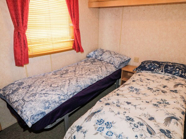 Quarto pequeno com uma cama de solteiro e janela coberta por cortinas vermelhas.