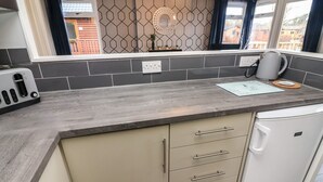 Uma cozinha moderna com azulejos cinzas, torradeira, chaleira e janela com vista para edifícios.