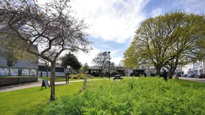 Um parque com grama verde, árvores, um banco e um coreto.