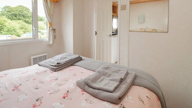 Quarto com cama, janela com cortinas, espelho e porta para outro cômodo.