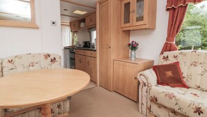 Interior compacto de uma motorhome, com mesa de jantar, sofá, armários de madeira e uma cozinha compacta.