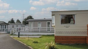 Fileira de casas móveis com área gramada na frente, caminho pavimentado e cerca.